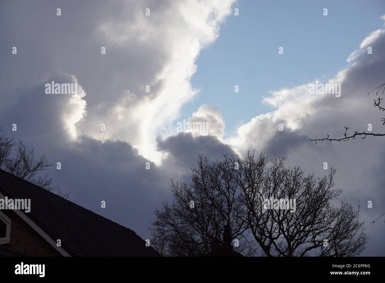Dark hail clouds and a piece of blue sky above the trees and a roof of ...
