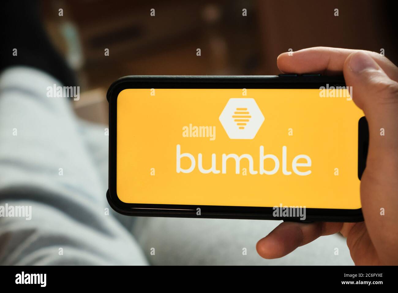 Bumble application on the smartphone in mans hand. Man laying and using ...