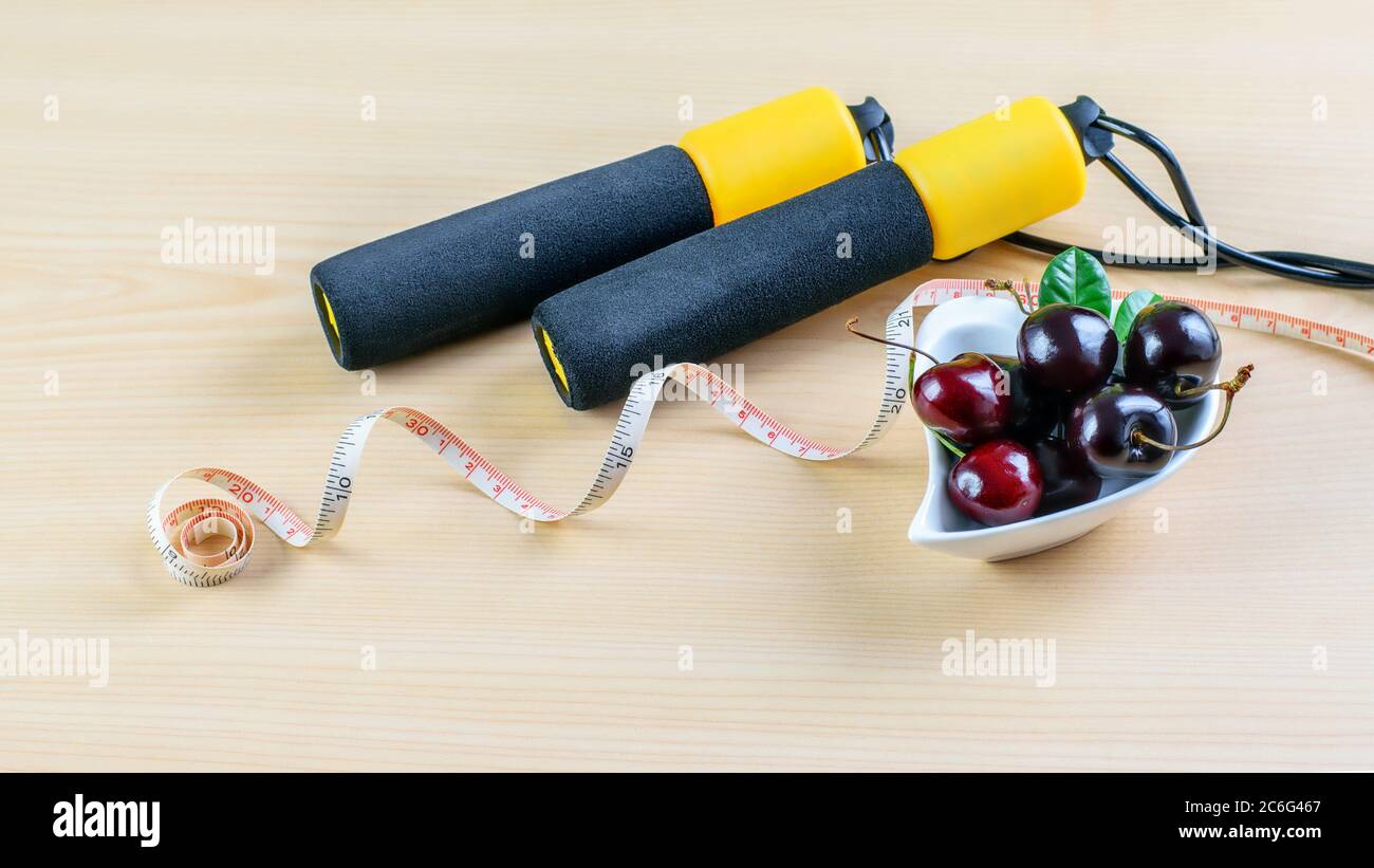 Jump rope, dosing tape and heap of fresh ripe cherries on the wooden ...
