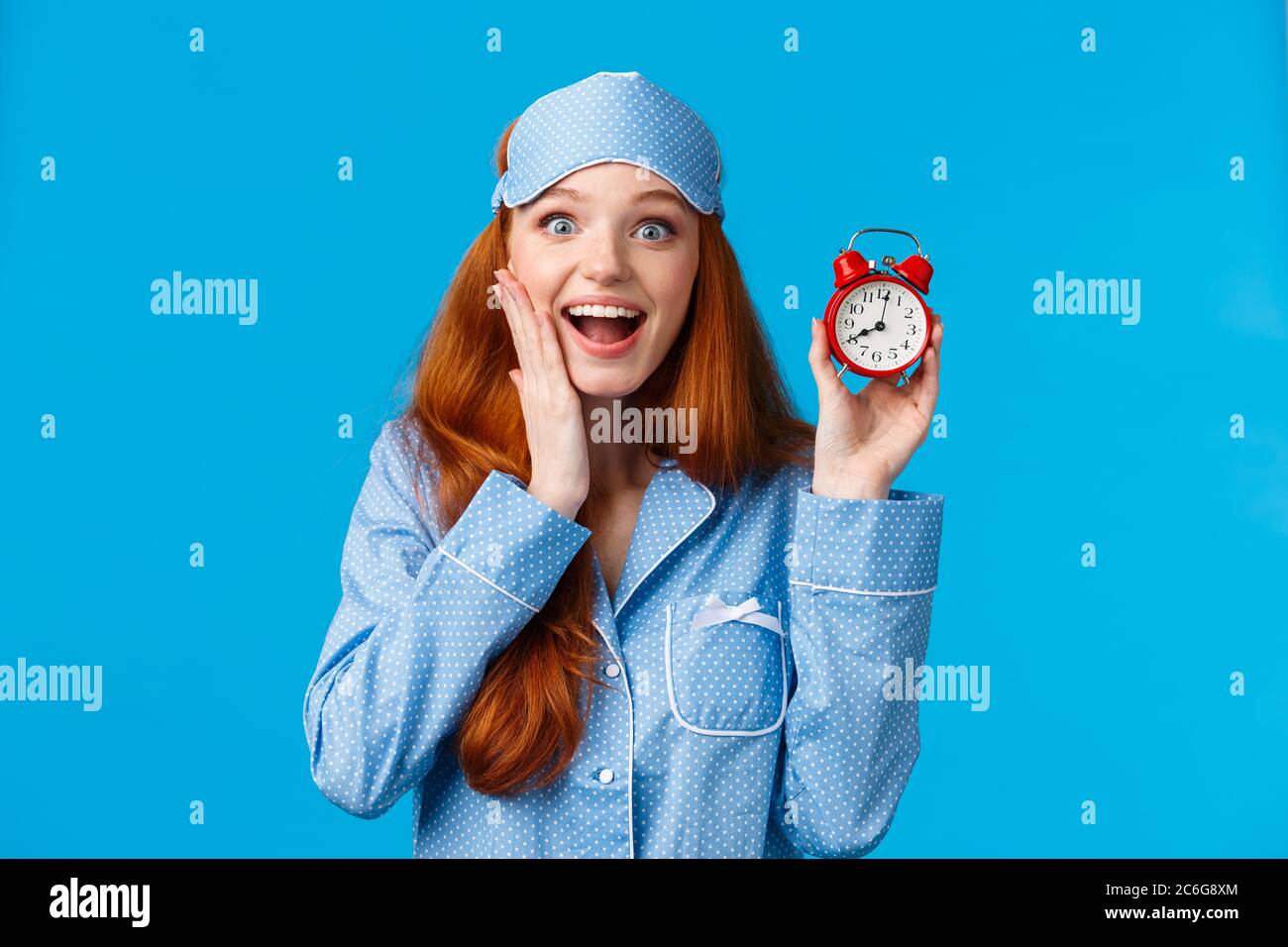 Excited young girl wake up on time, holding red cute clock set alarm ...