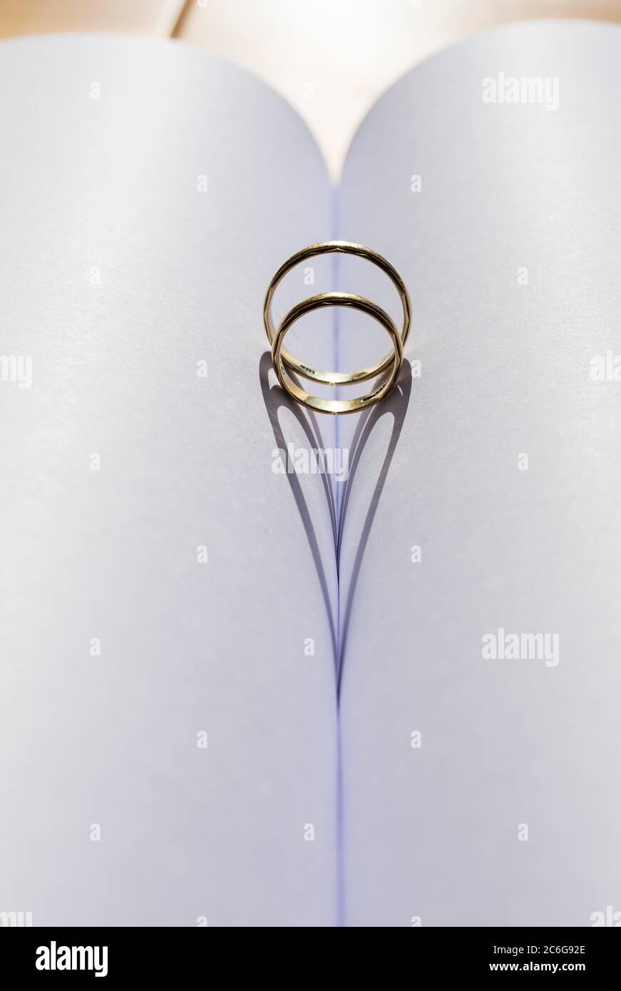 Two wedding rings in the fold from an empty book, heart-shaped shadow ...