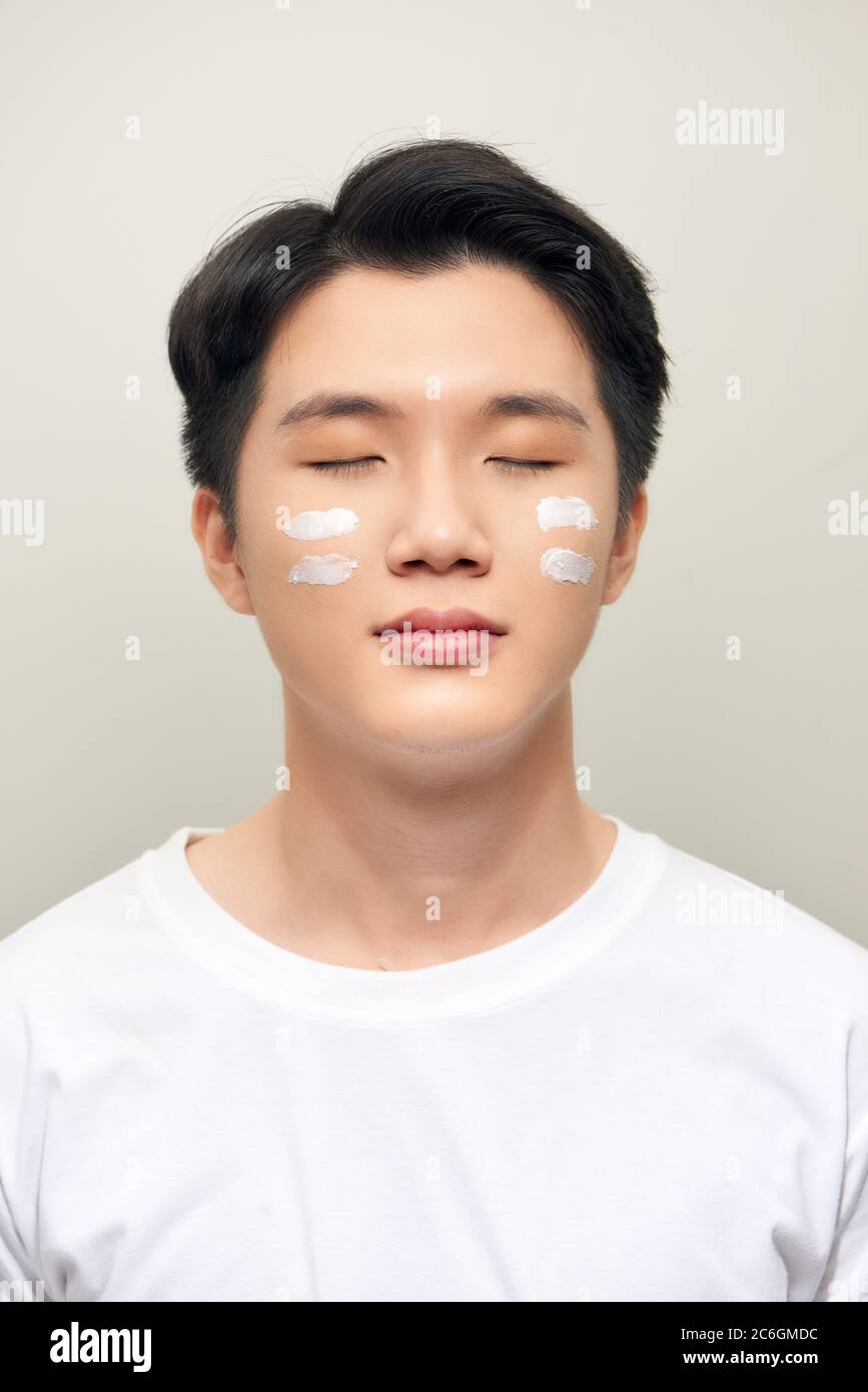 Skin care. Portrait of handsome young man applying cream to his face ...