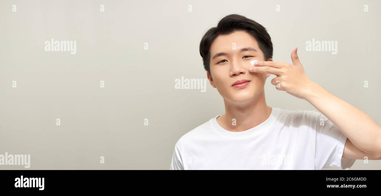 Skin care. Portrait of handsome young man applying cream to his face ...