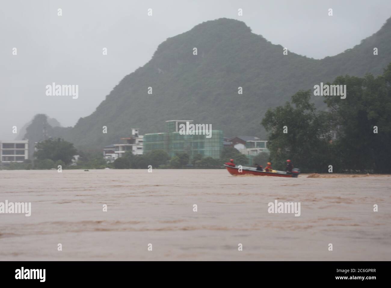 People sit in a boat to mobile around in a village flooded by heavy ...