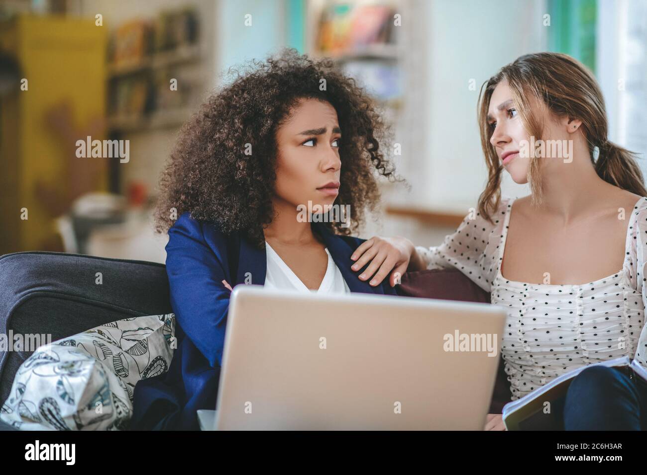 Two sad girls sitting on couch looking at each other Stock Photo - Alamy