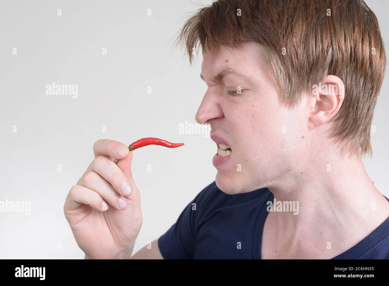 Portrait of stressed young man eating chili pepper Stock Photo - Alamy