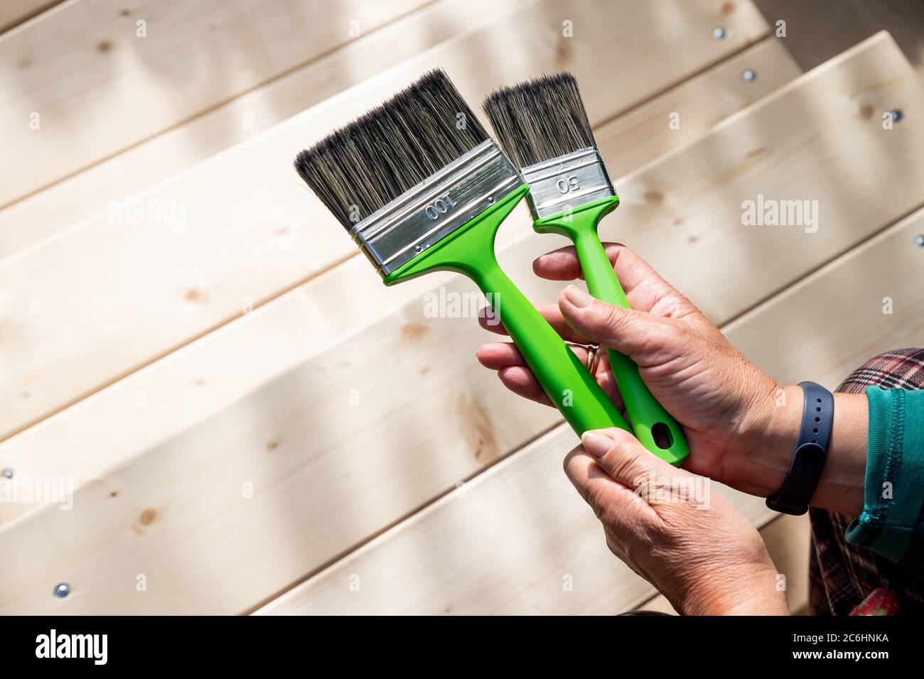 Active senior woman painting some pieces of wood, timber by brown paint ...