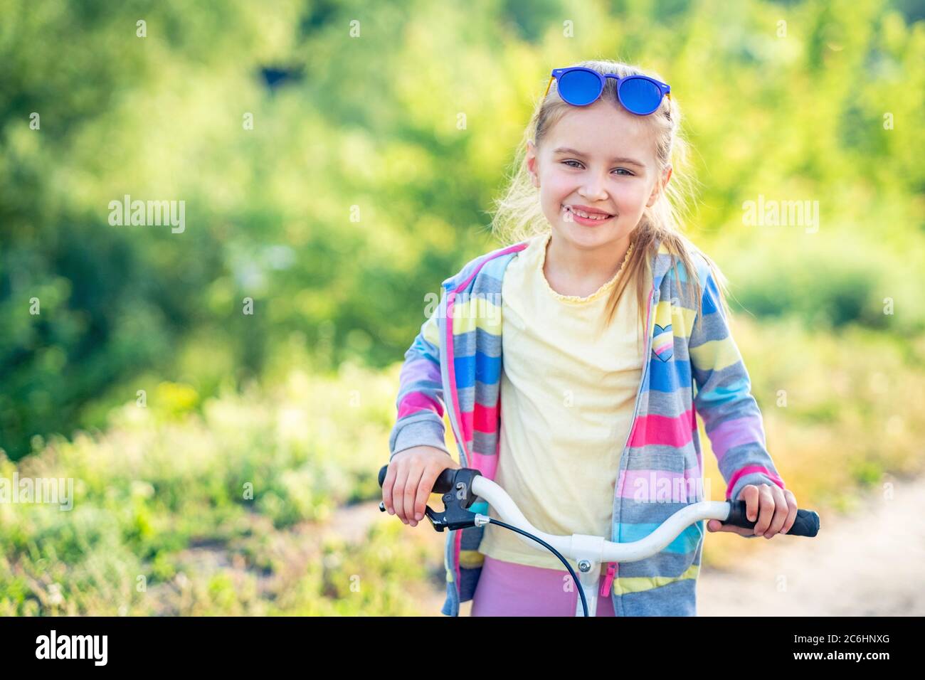 Smiling girl riding small modern bike with colorful jacket outdoors ...