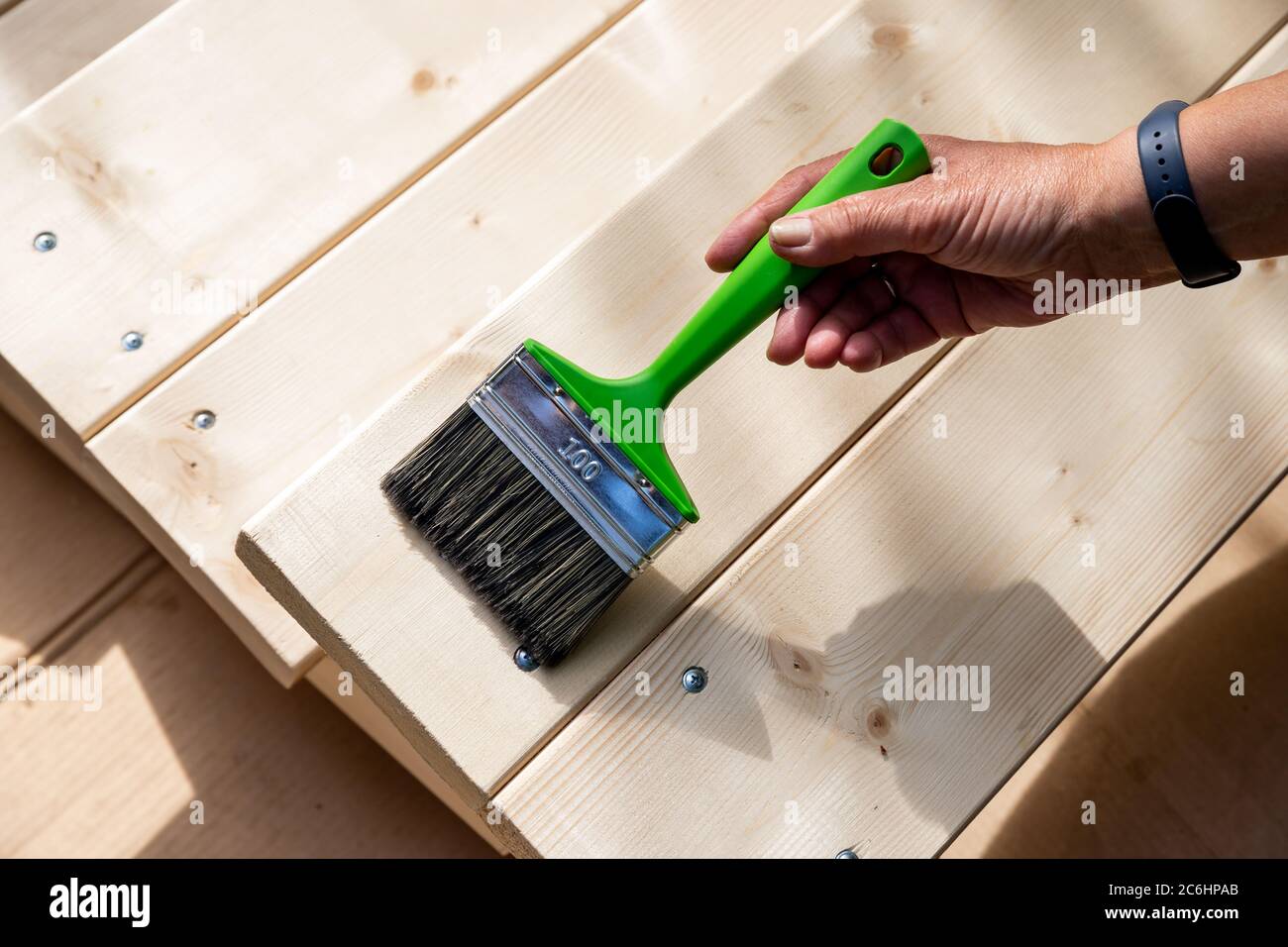 Active senior woman painting some pieces of wood, timber by brown paint ...