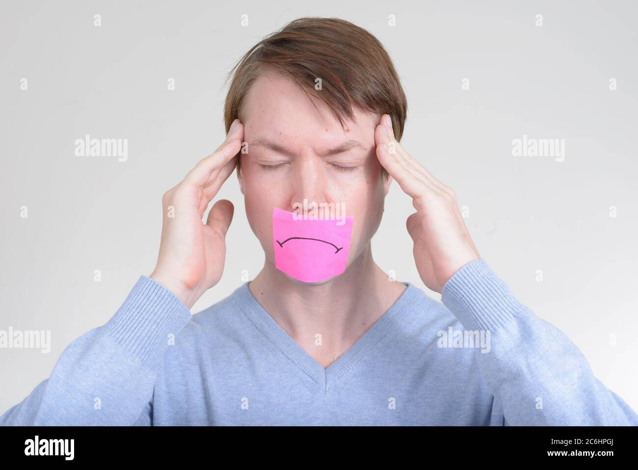 Portrait of stressed young man with frowning sticker on mouth having ...