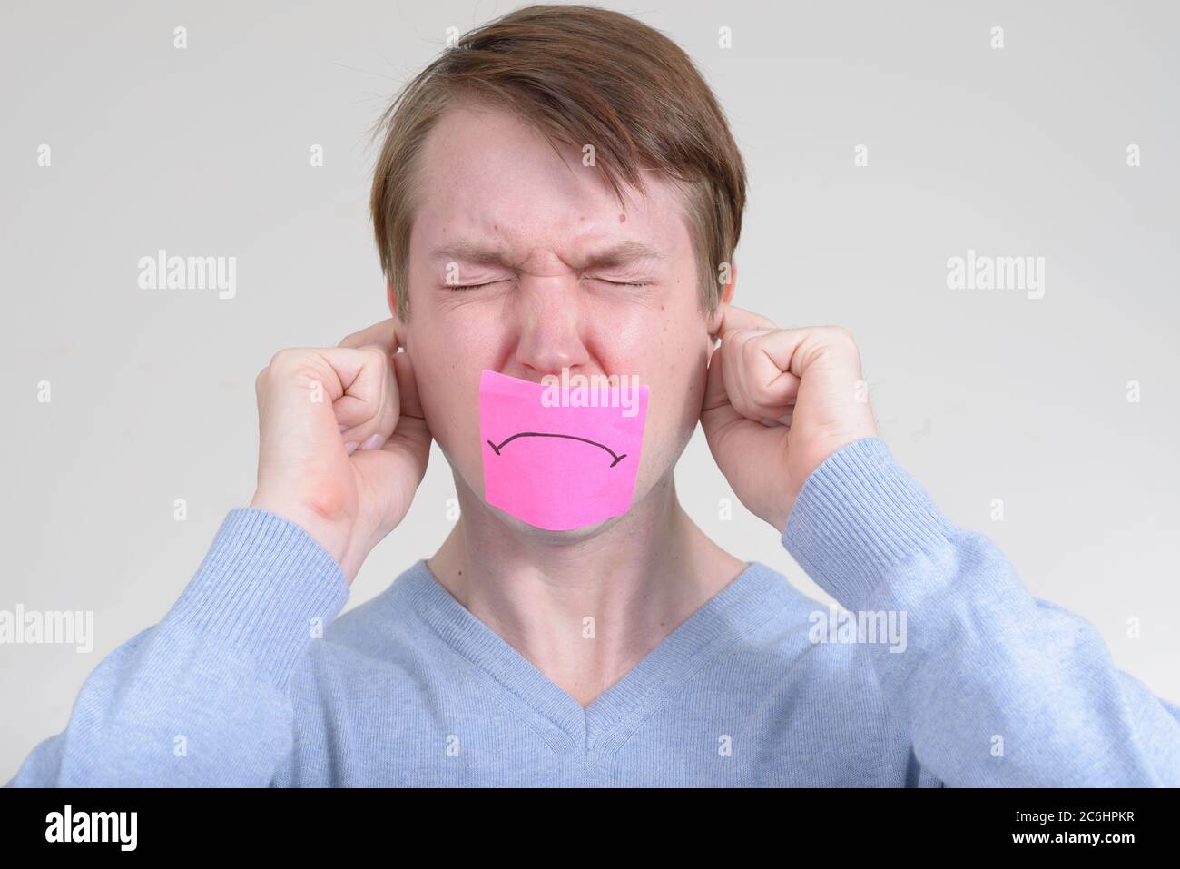 Portrait of stressed young man with frowning sticker on mouth covering ...