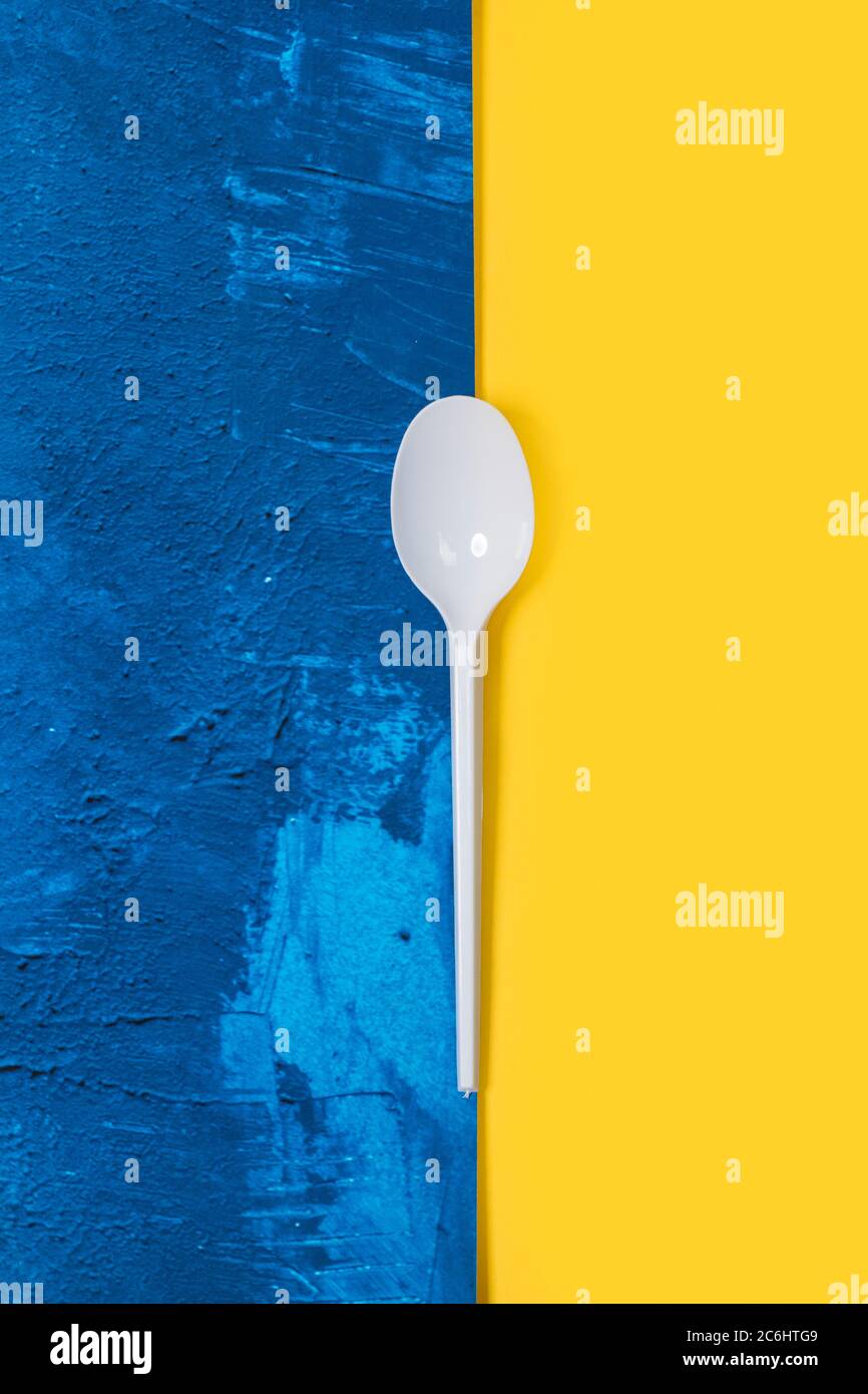 Disposable white plastic spoon on a classic blue and yellow background ...