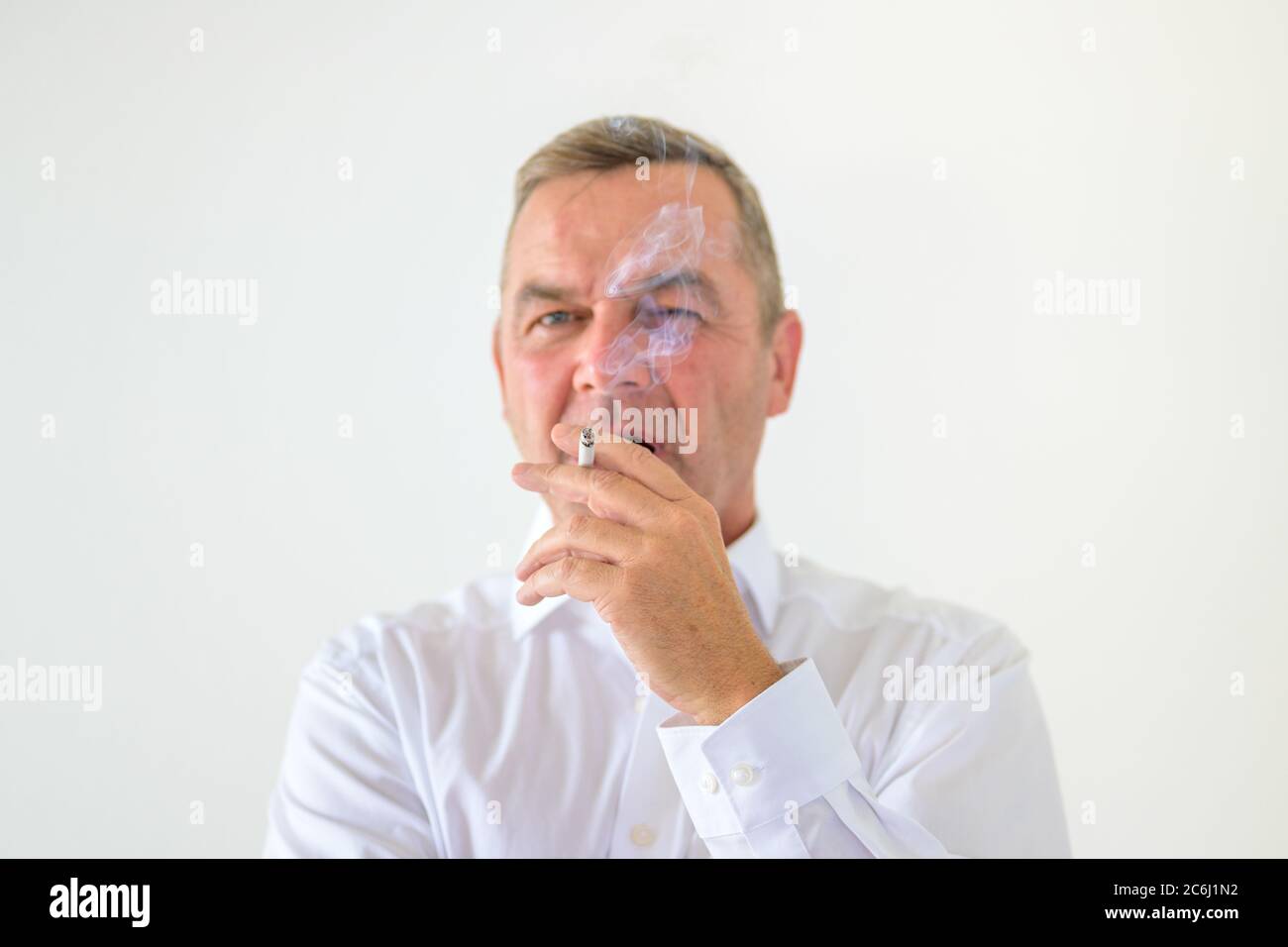 Thoughtful man puffing on a cigarette squinting in concentration behind ...