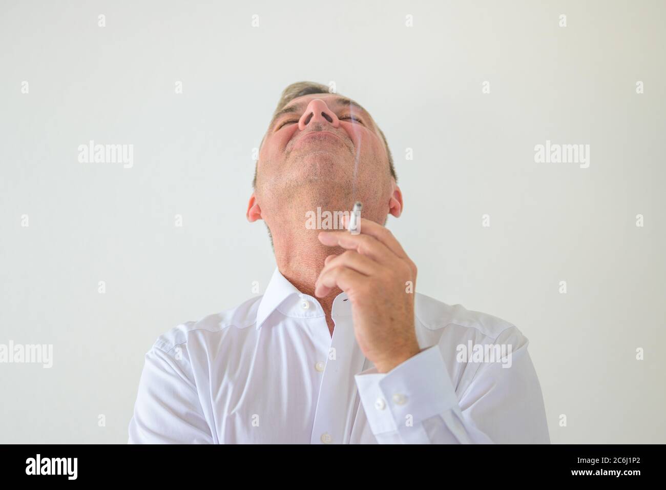 Middle-aged man enjoying smoking a cigarette tilting back his head as ...