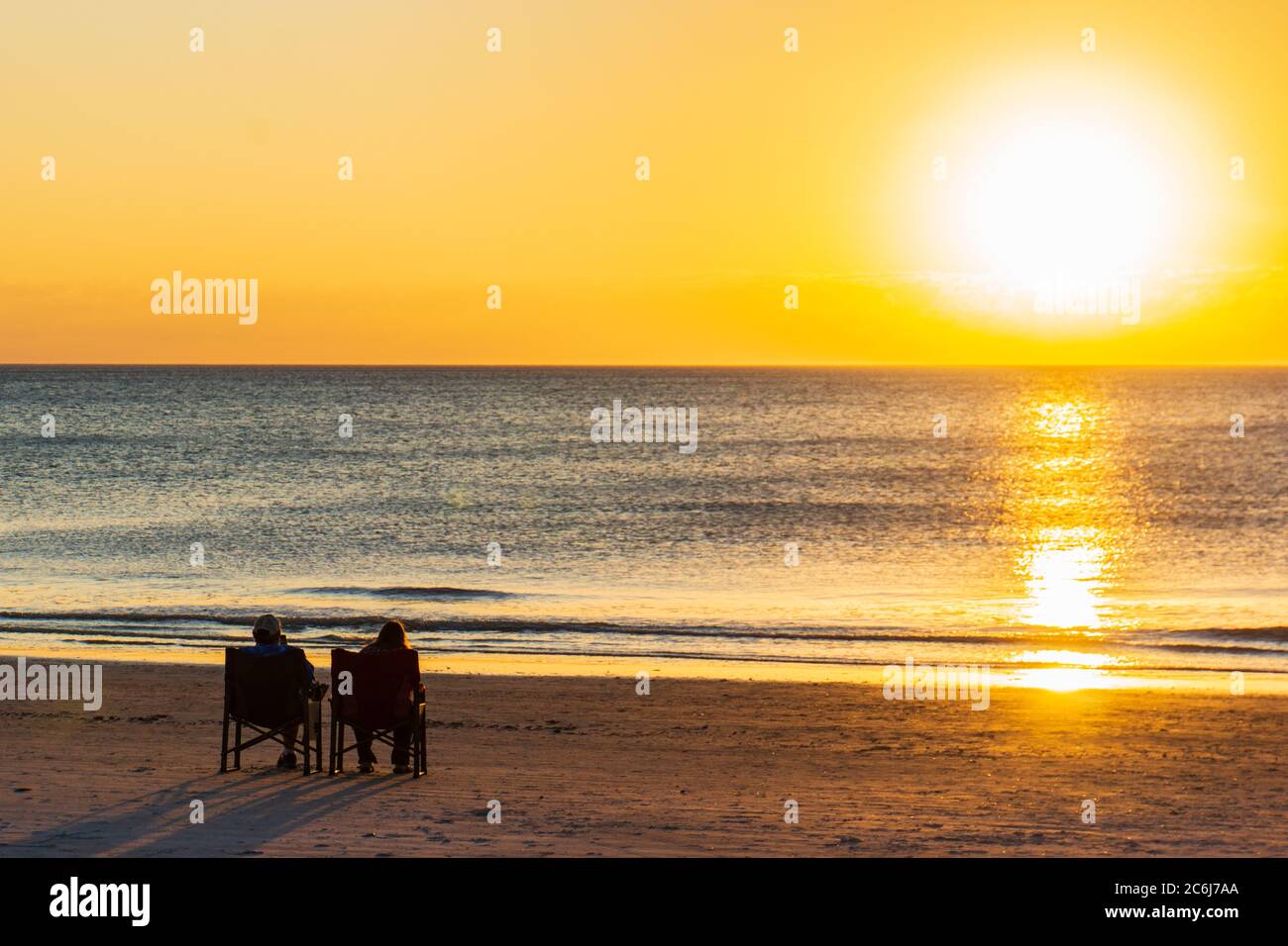 two people sitting on beach enjoying the sunset Stock Photo - Alamy