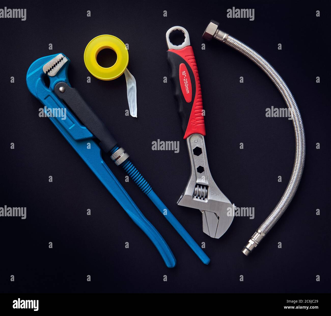 Tools, adjustable wrenches, flexible hose and thread seal tape on dark ...