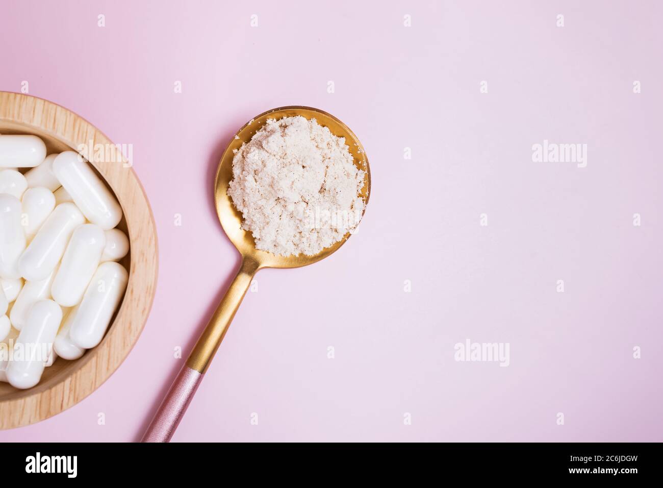 White powder in a spoon and pills on pink background. Dietary ...
