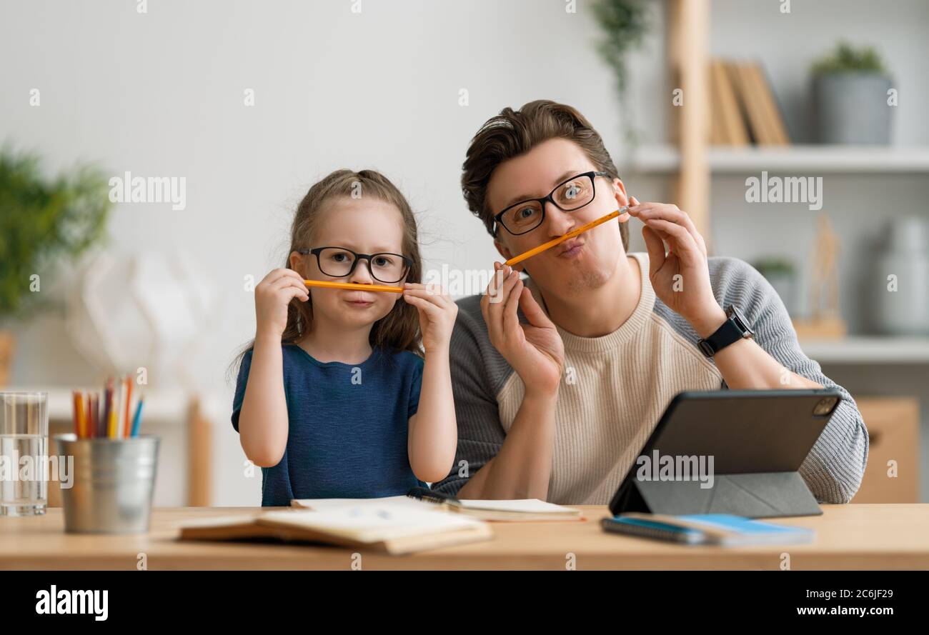 Back to school. Happy child and adult are sitting at desk. Girl doing ...