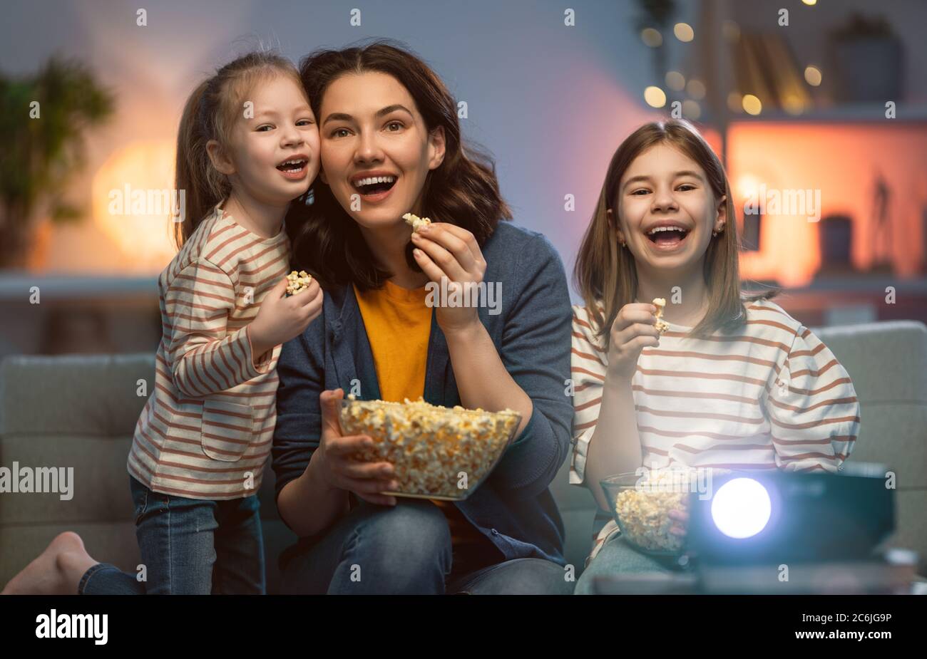Happy family watching projector, TV, movies with popcorn in the evening ...