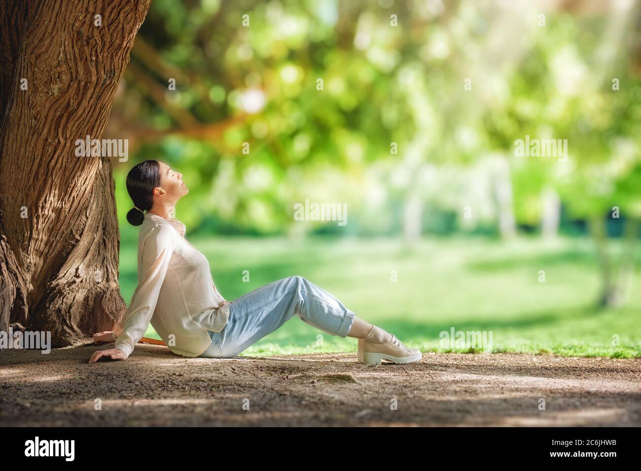 Young woman relaxing under big tree in the park outdoors Stock Photo ...