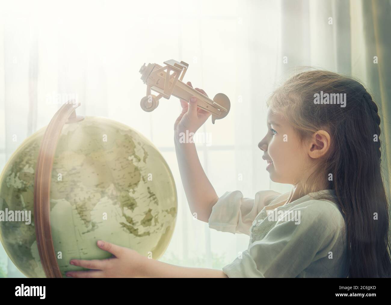 Go on an adventure! Cute child girl playing with toy airplane and globe ...