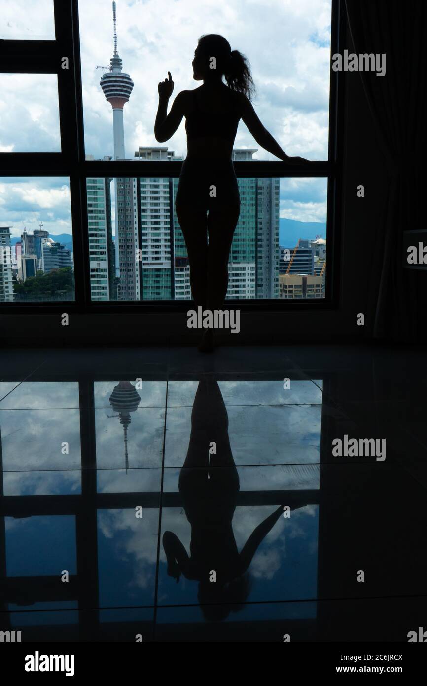 A slender girl is looking at the city through a large window. High ...