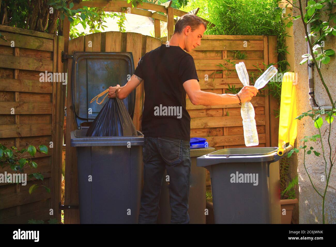 Person performing a selective sorting of household waste in recycling bins. Man putting plastic ...
