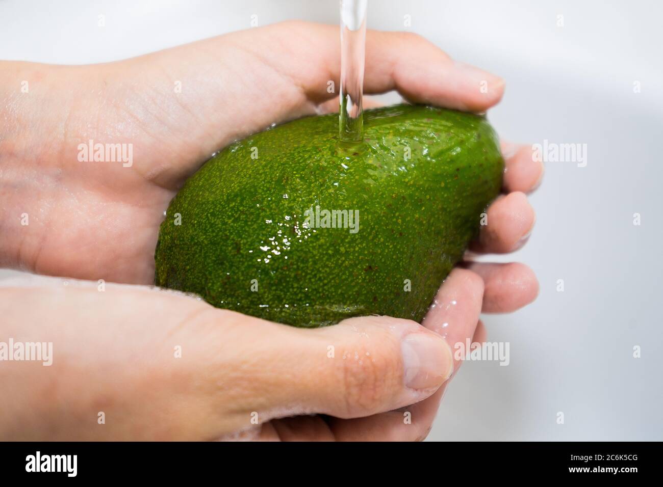 washing fruits under running water. Hands and avocado under a stream of ...