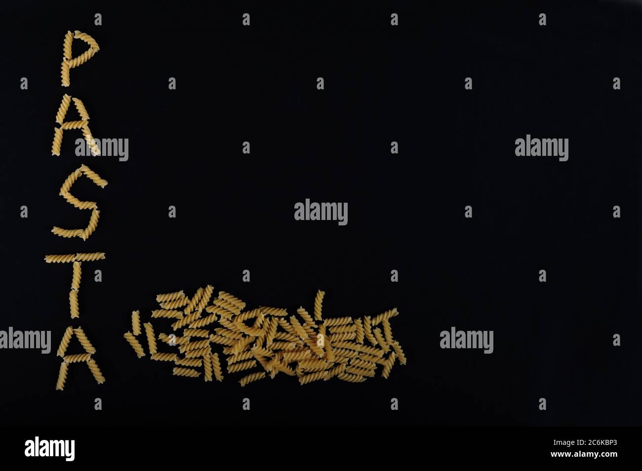 The word PASTA written vertically in pasta screws on black surface ...
