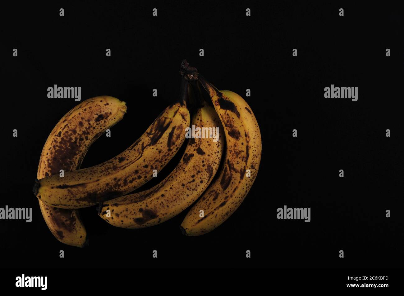 Four over ripe bananas on black surface. High angle vertical shot with ...