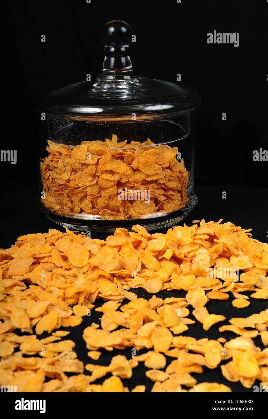 Glass jar with corn flakes. Container behind corn flakes spread out on ...