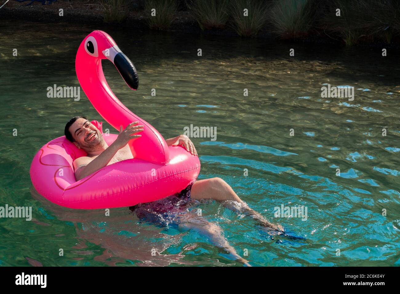Cute and funny man enjoying on his inflated pink flamingo in sunny day ...