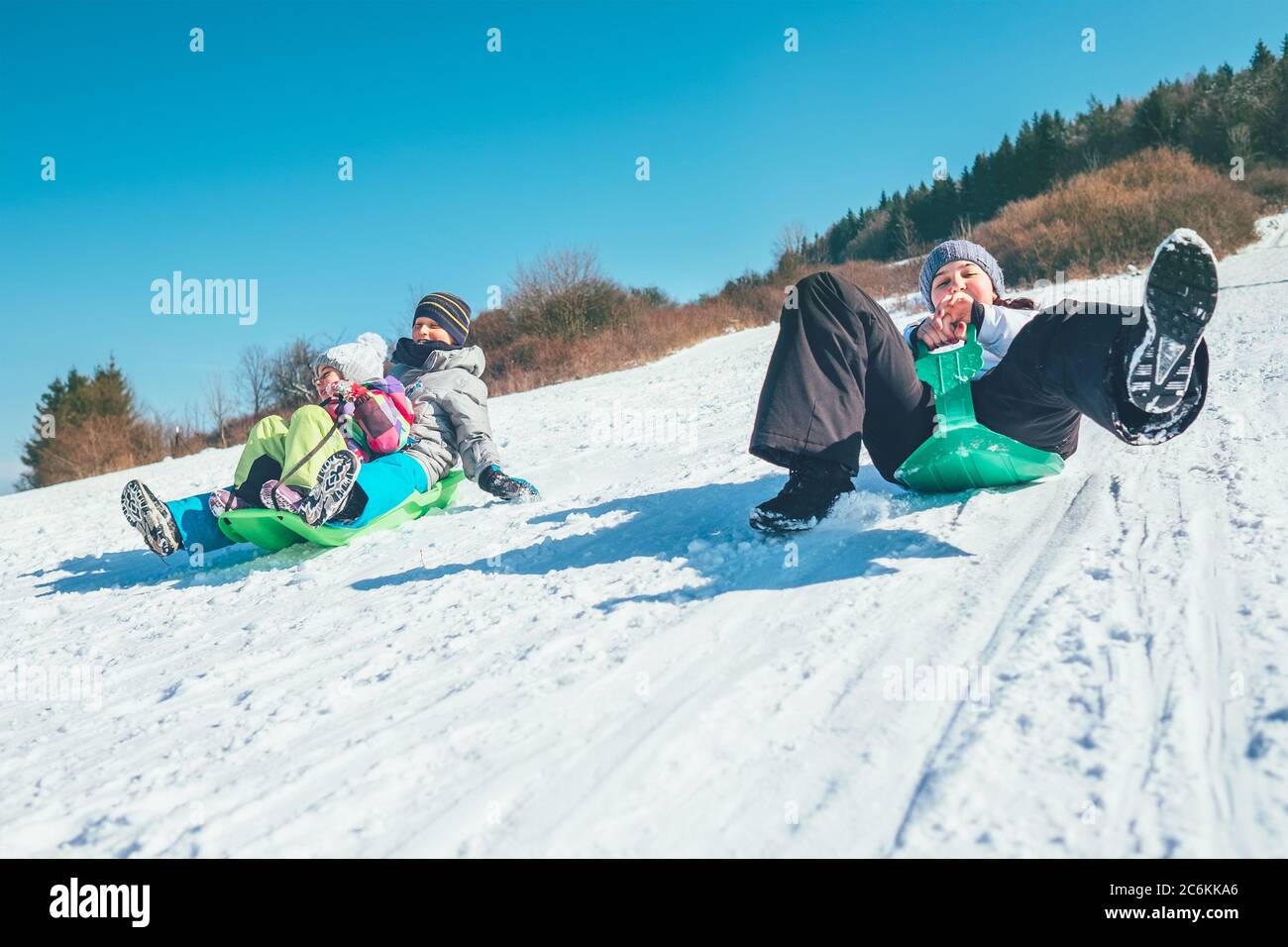 Happy laughing kids sliding down from the snow slope riding sleighs ...