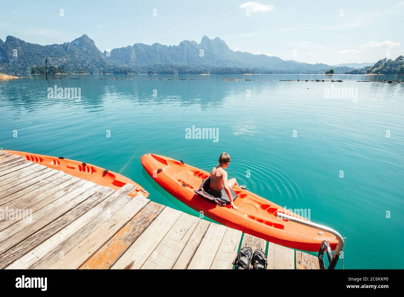 Little boy sitting on orange kayak near the pier and dangling feet ...