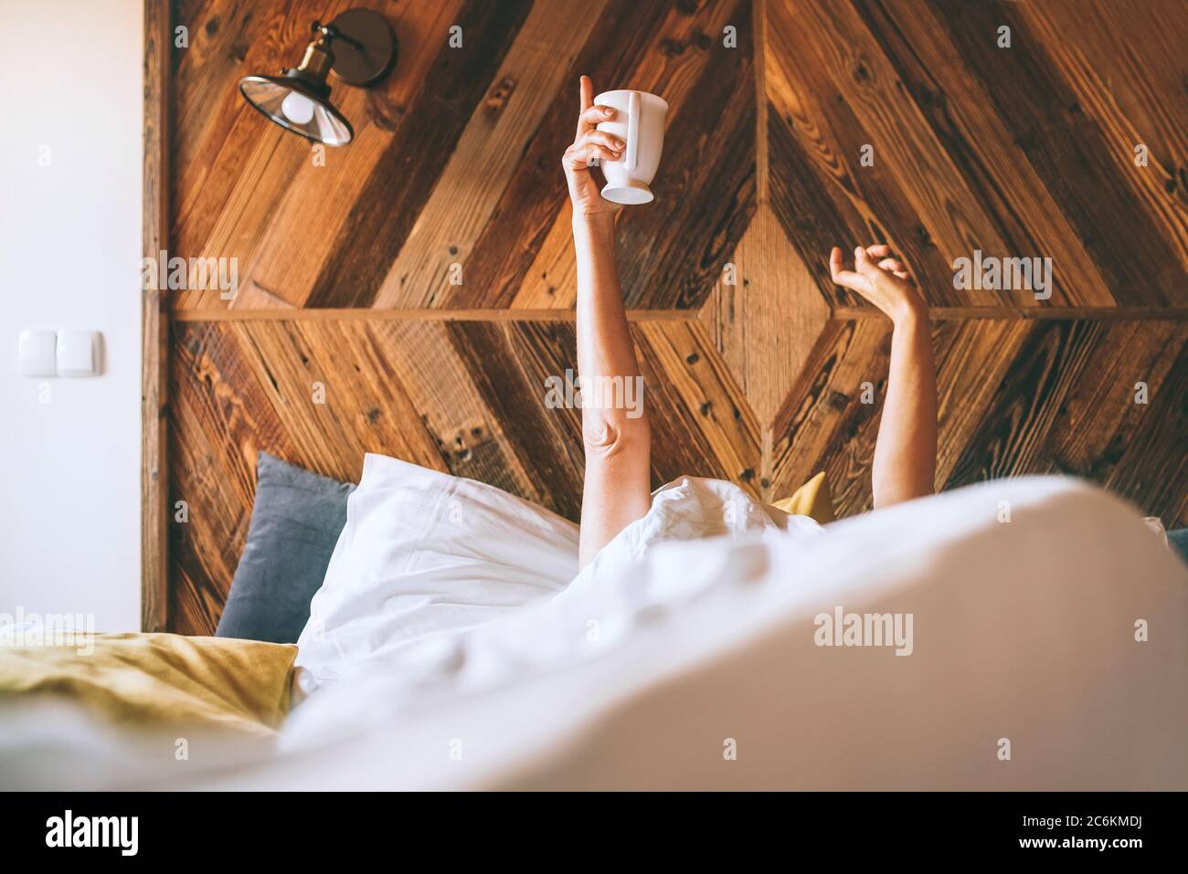 Lazy female lying under the white blanket on the linen bed and holding ...