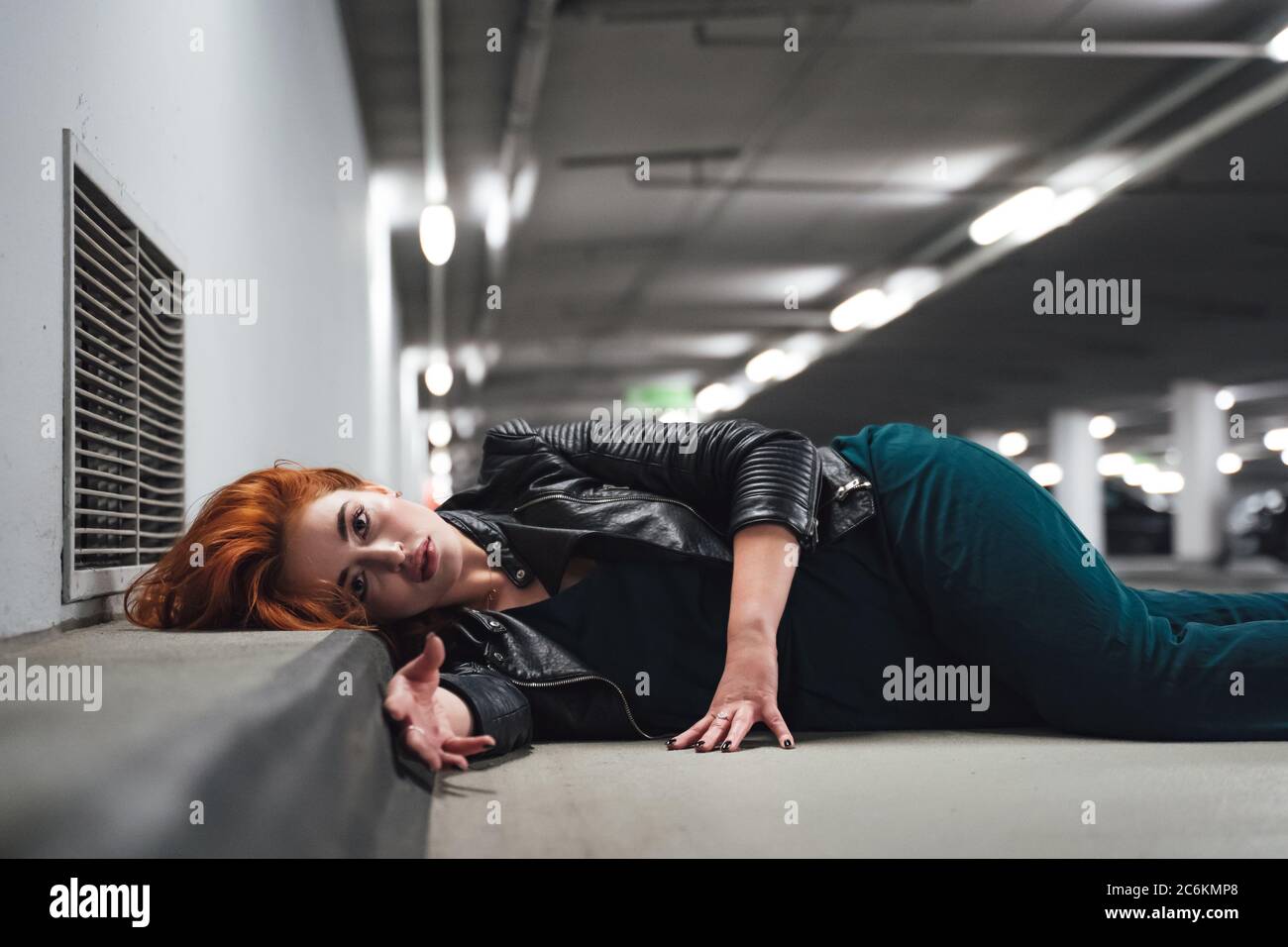Attractive millennial girl with head on curb laying on floor in parking ...