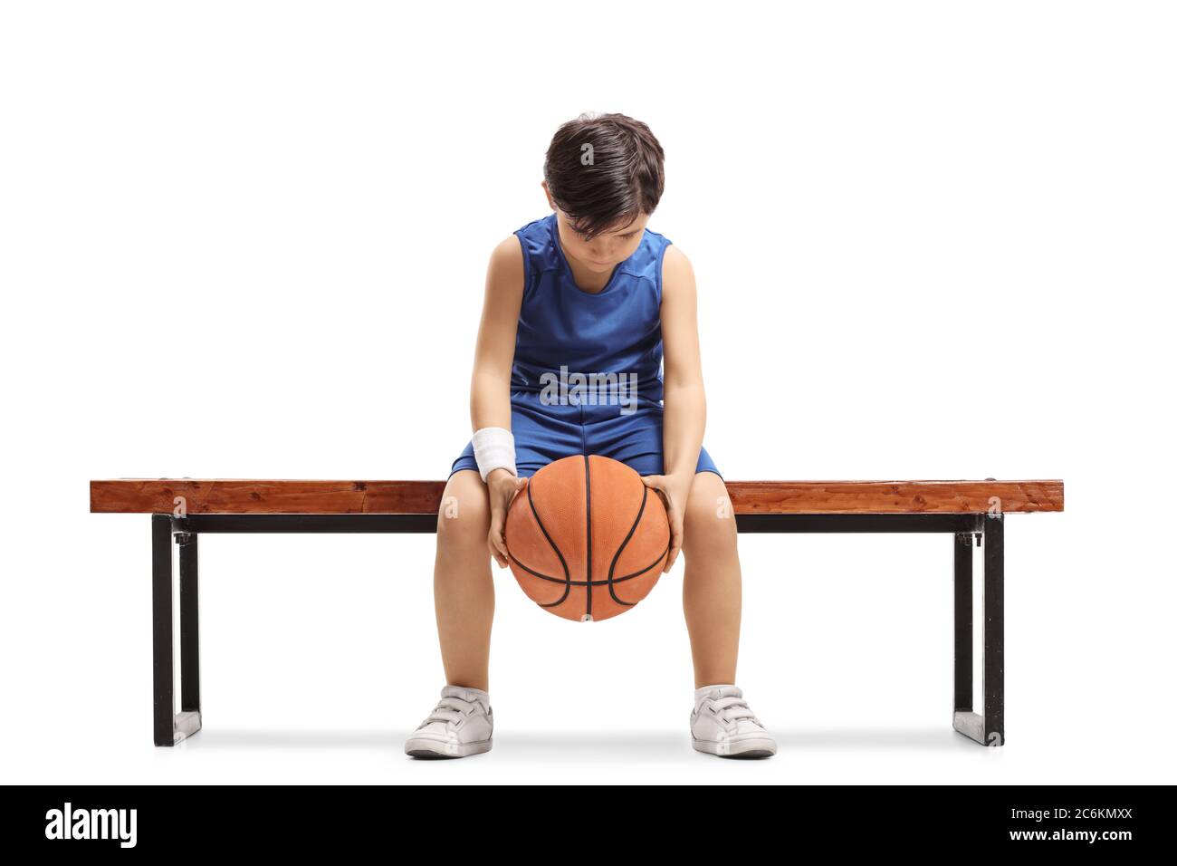 Sad little boy sitting on a bench with a basketball isoalted on white ...