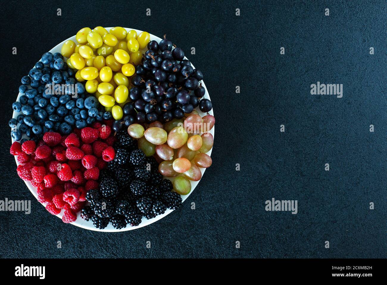 Mix of colored berries in a round plate divided by triangles. Stylish ...
