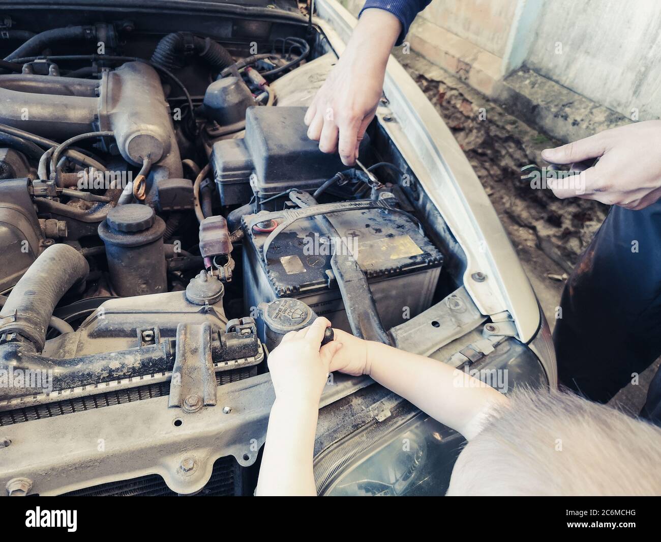 Litte boy is helping his fater to repair the car in his home garage ...