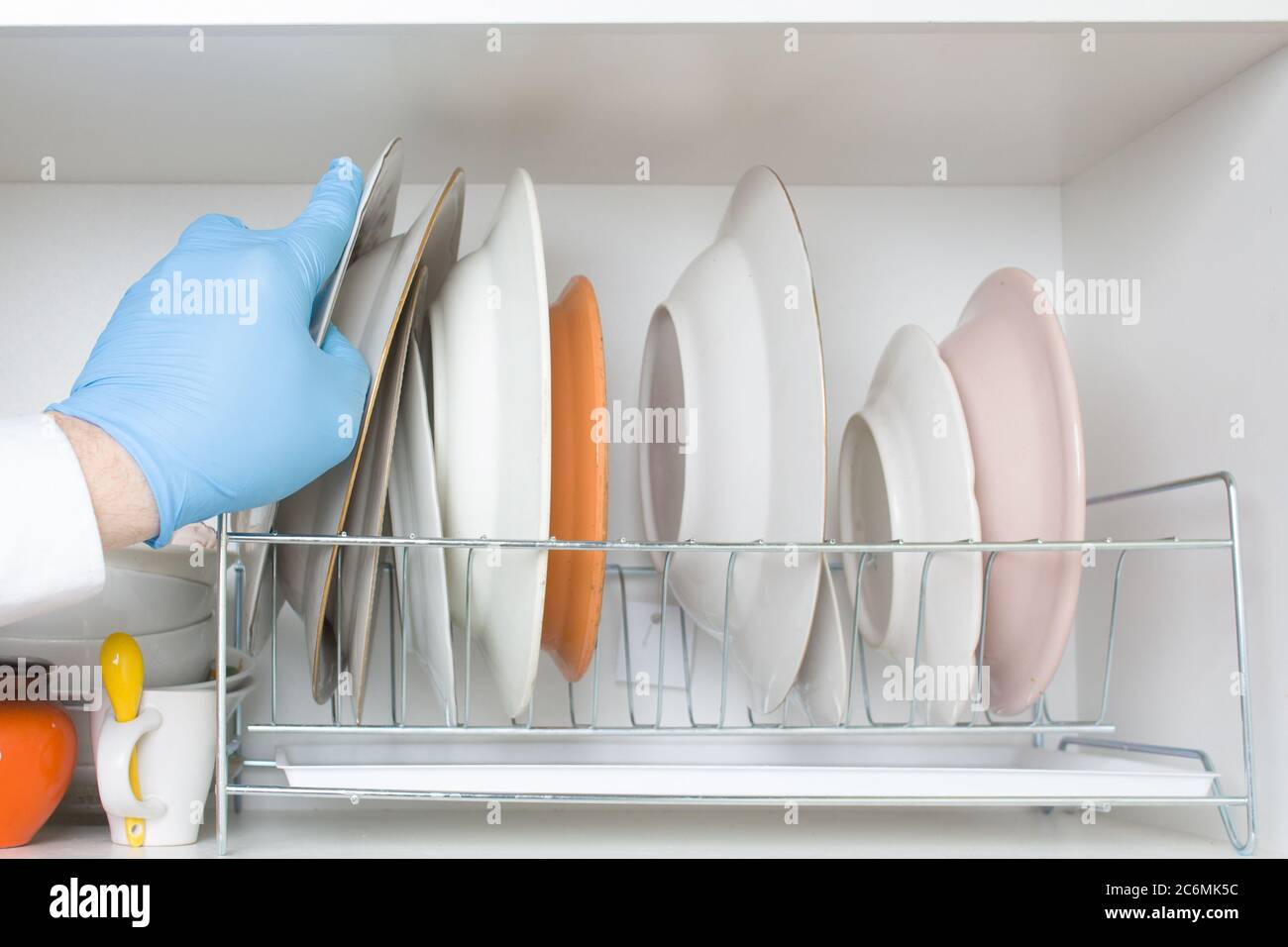 a blue gloved hand places a clean plate on the drying table Stock Photo ...