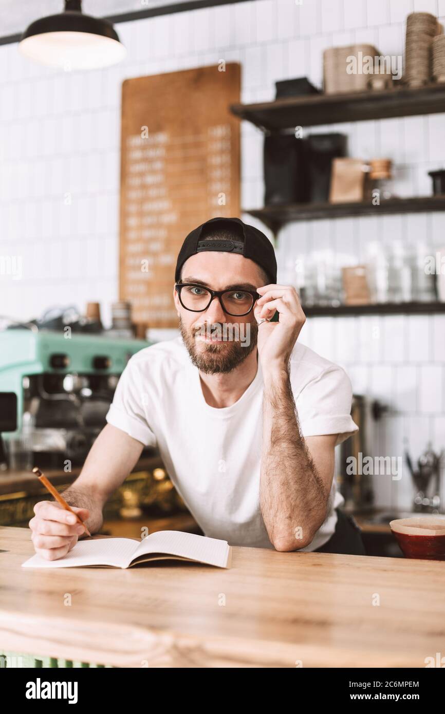 Smiling man in eyeglasses and cap standing behind bar counter with ...