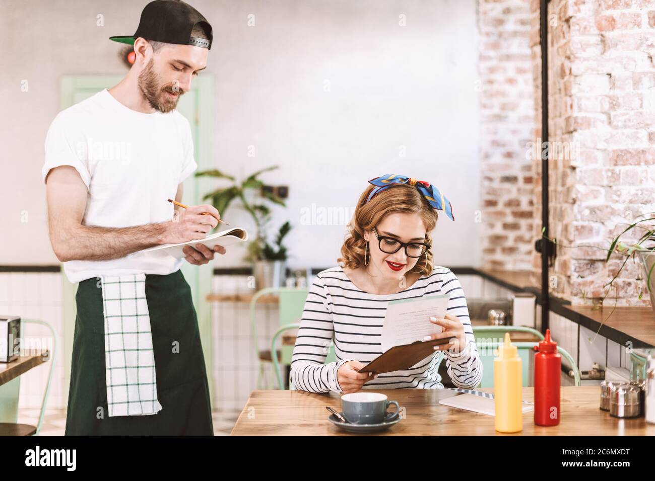 Beautiful lady in eyeglasses sitting at the table with menu in hands ...