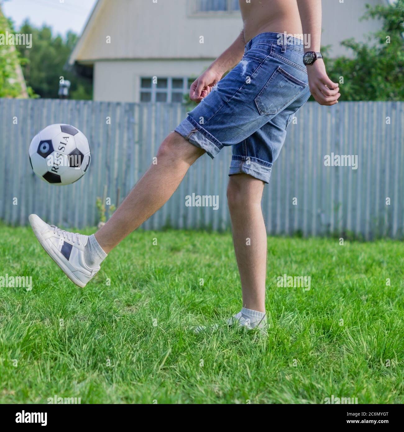 young man in denim jeans and white sneakers playing football ball ...