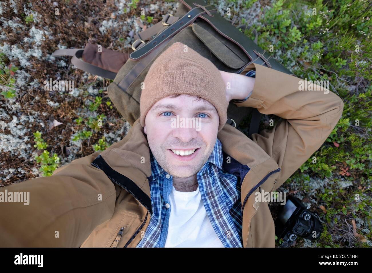 young man laying down on the ground of a forest and making a selfie ...