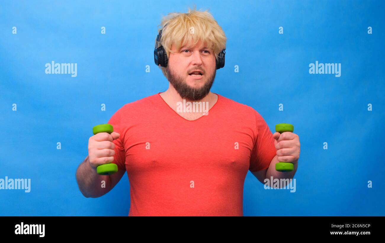 Funny fat man freaky in a wig and a pink t-shirt with dumbbells doing ...