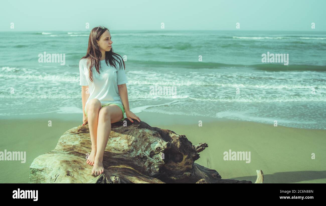 Relaxed woman sitting on log and looking away. Female tourist resting ...