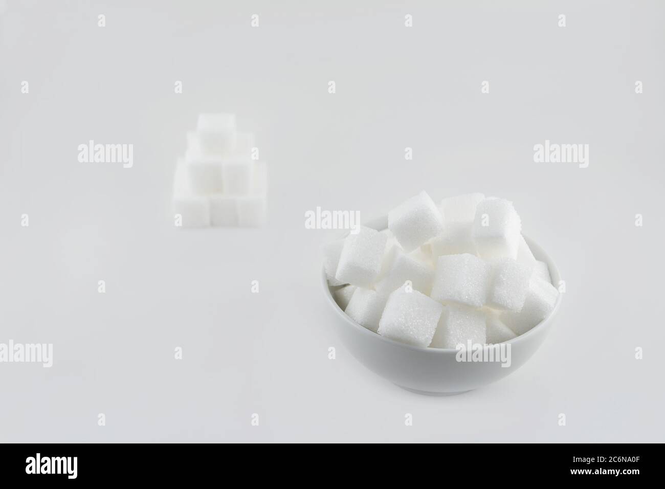 Sugar cubes in a white bowl, with a few sugar pieces stacked next to ...
