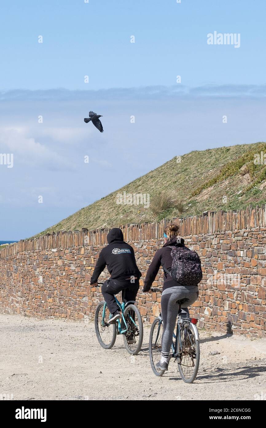 A crow flying overhead as two people cycle along the coastal path at ...