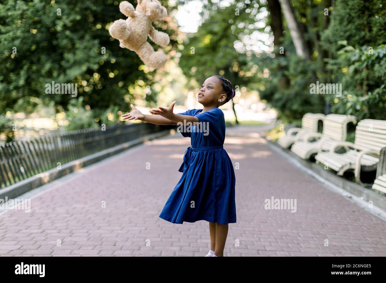 Portrait of happy little African girl child in green city park throwing ...