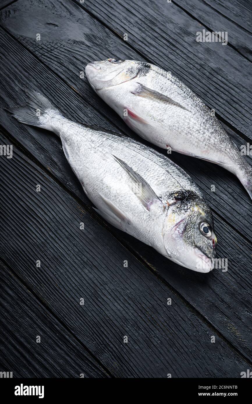 Raw whole pair dorado or sea bream fish ob black wooden table side view ...